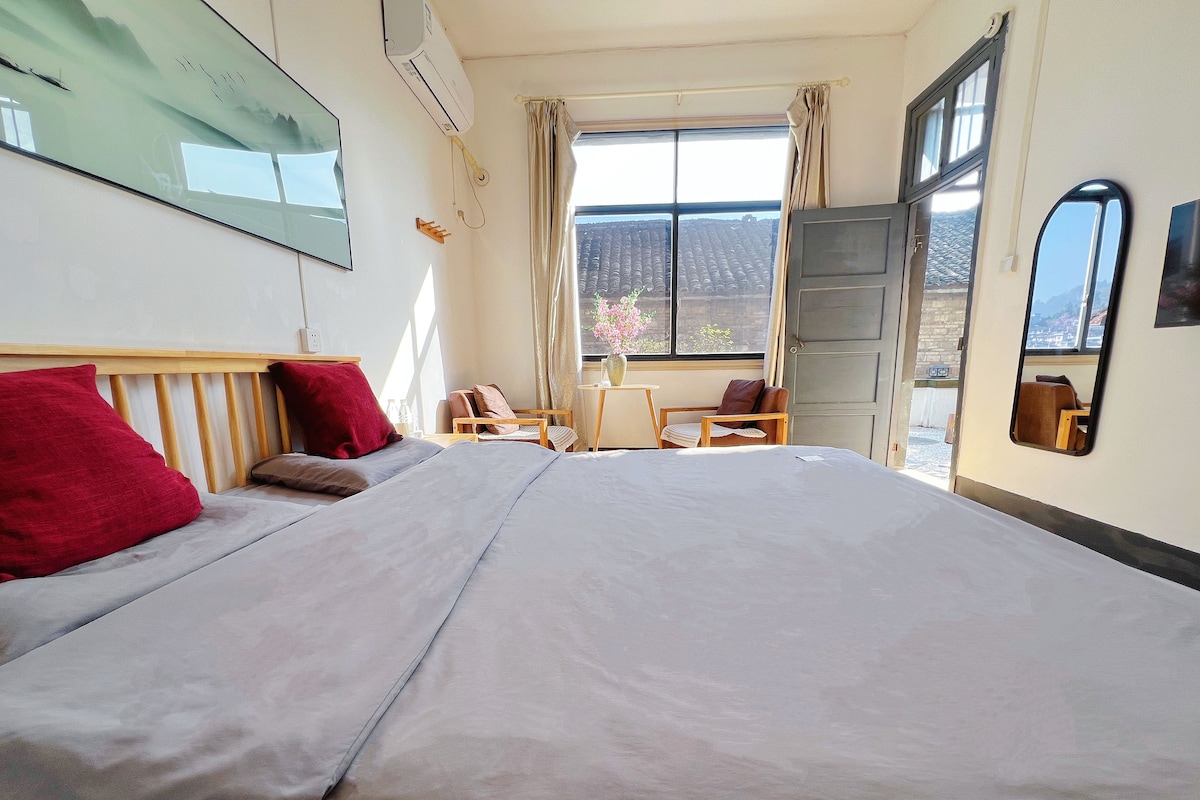 Quarto de hotel com cama, escrivaninha, cadeira e janela com vista.