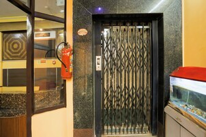 Um elevador com portão de metal, extintor de incêndio fixado na parede e um aquário à direita.
