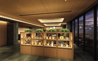 Interior moderno com balcão de recepção de madeira exibindo diversos frascos e objetos decorativos, teto com iluminação embutida e uma grande janela com vista para o exterior.