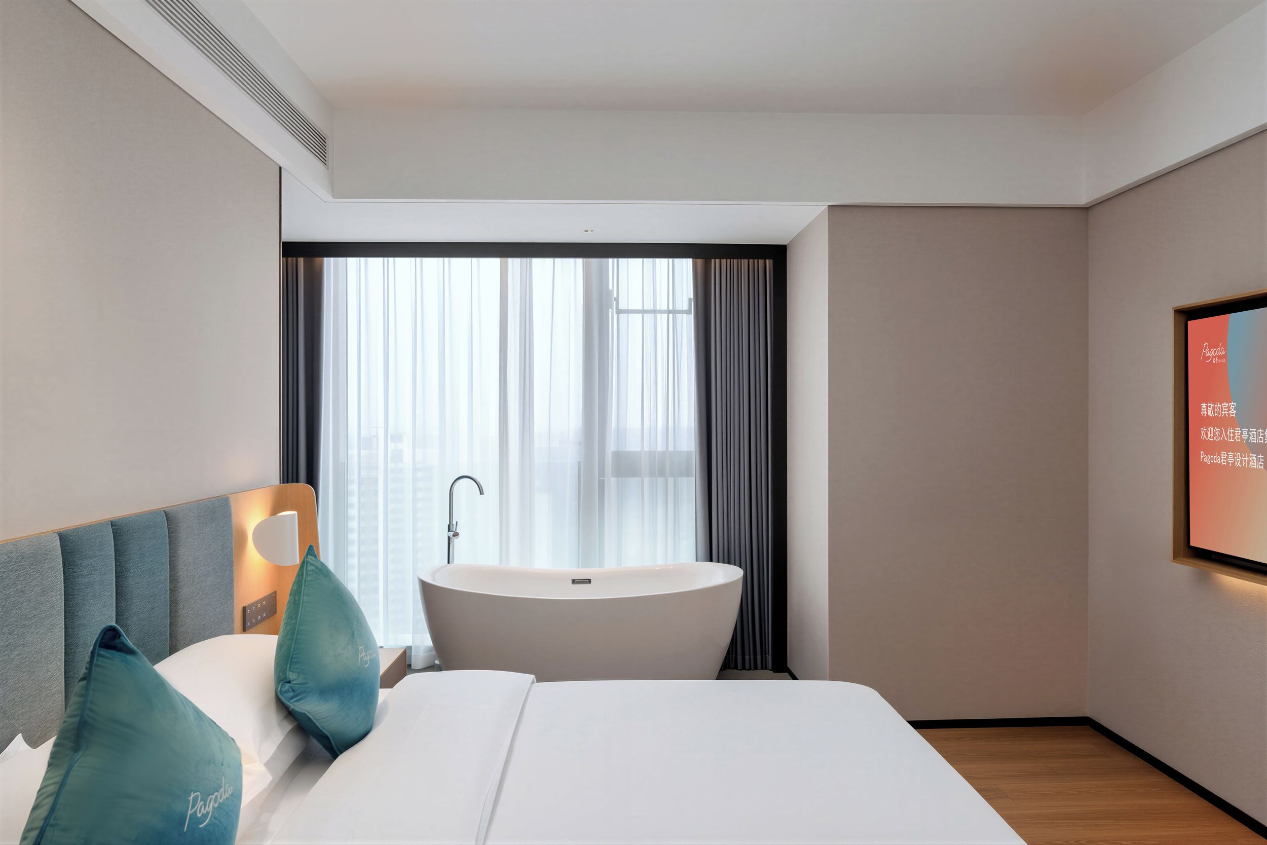Quarto de hotel com cama grande, banheira, janela com cortinas e TV fixada na parede.