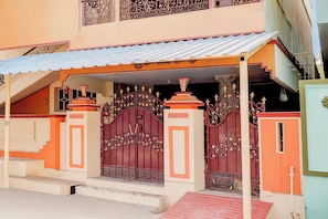 Edifício residencial com portão e escadaria que dá acesso à entrada, e cobertura metálica.