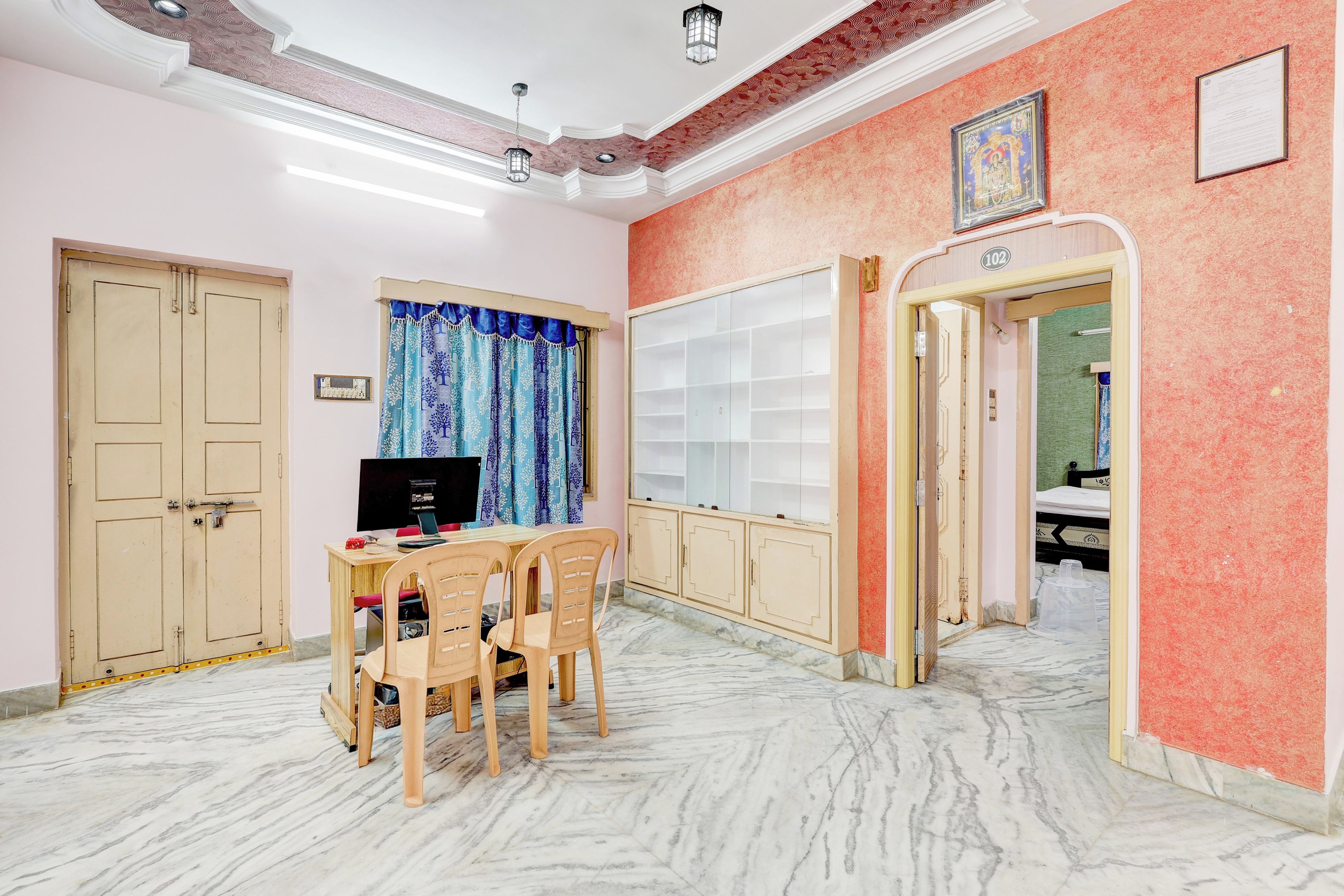 Quarto com piso de mármore, uma escrivaninha com computador, duas cadeiras, televisão e guarda-roupa.
