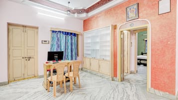 Quarto com piso de mármore, uma escrivaninha com computador, duas cadeiras, televisão e guarda-roupa.