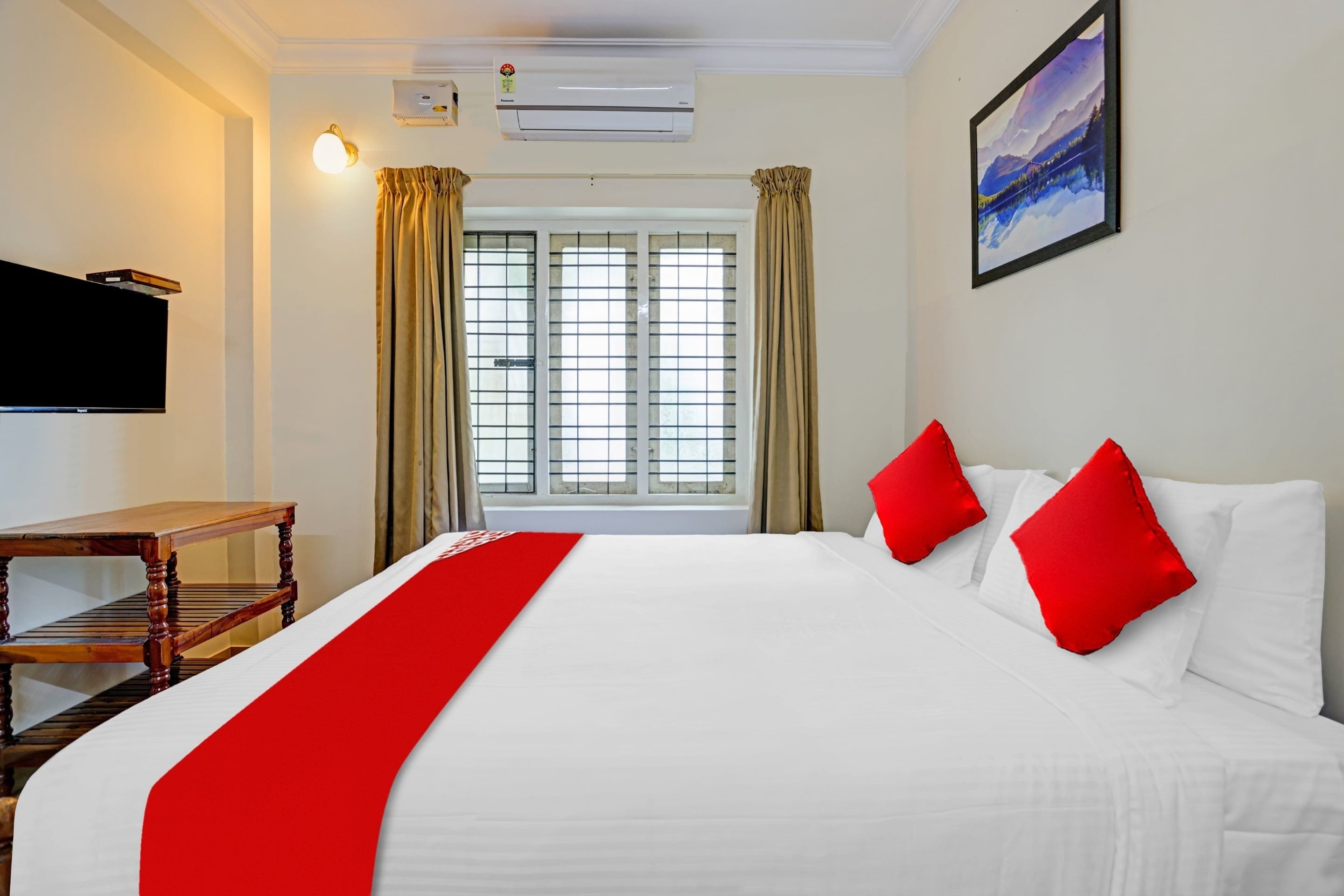Quarto de hotel com uma cama grande, televisão de tela plana, mesa de cabeceira de madeira e um quadro na parede.