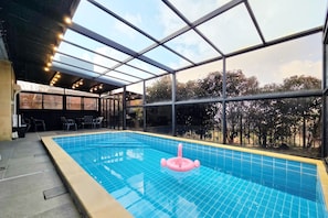 Uma piscina interna com paredes de vidro transparente, piso revestido e um flutuador rosa.