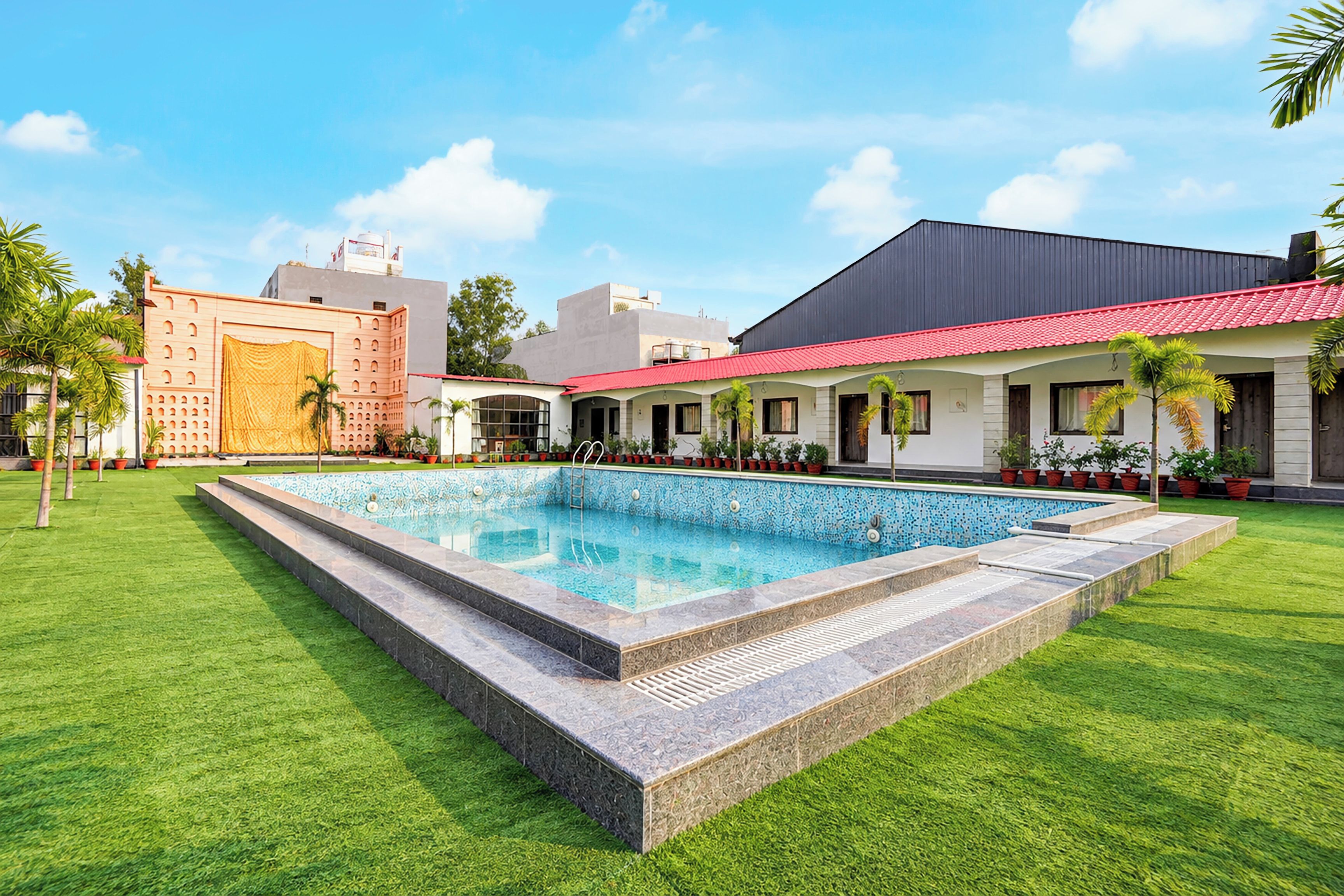 Piscina com deck revestido, cercada por gramado bem cuidado e plantas em vasos.