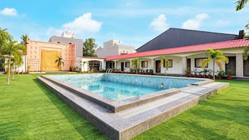 Piscina com deck revestido, cercada por gramado bem cuidado e plantas em vasos.