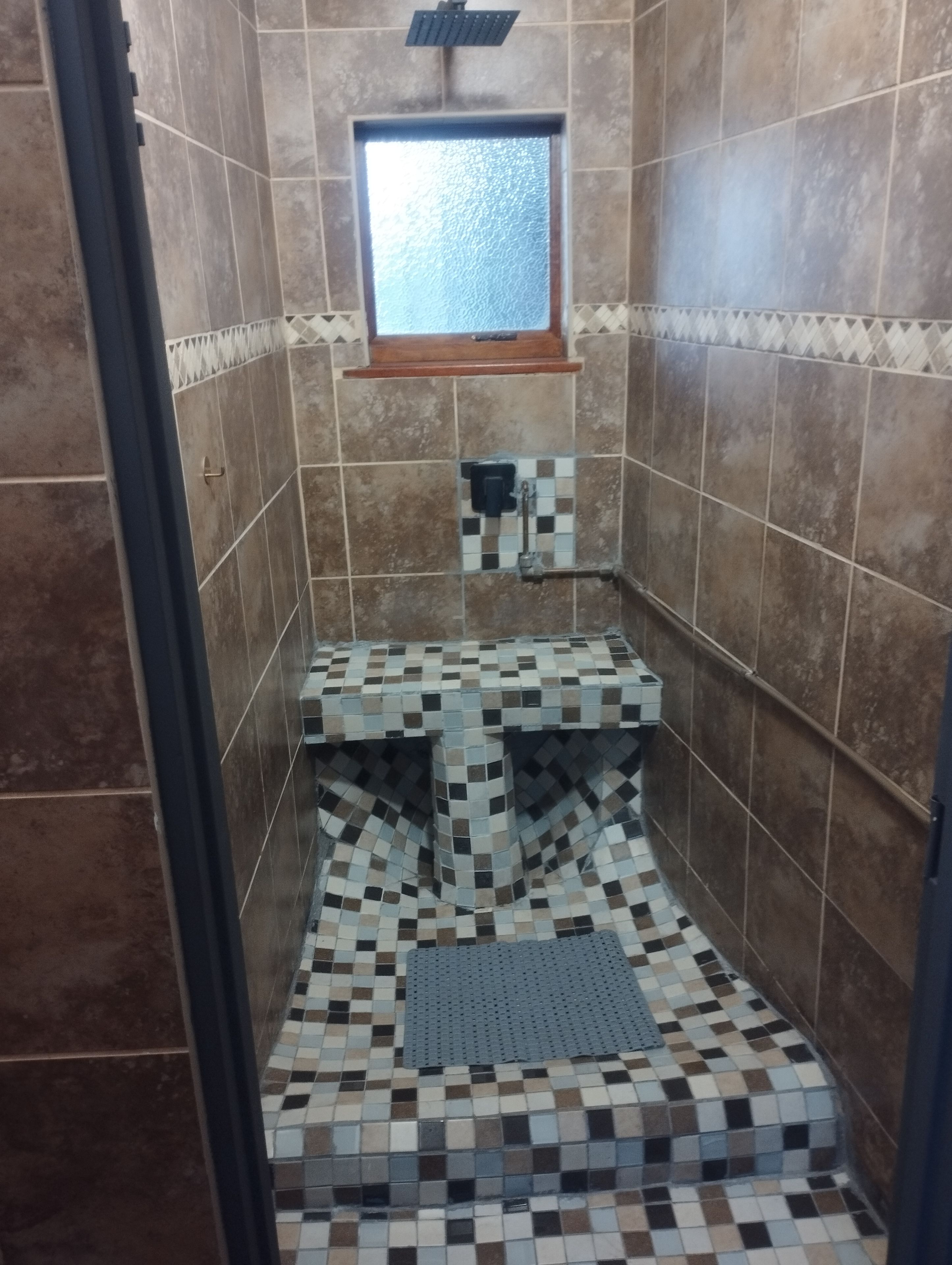 Pequeno espaço de chuveiro revestido com azulejos, com uma janela sobre a pia e chão em azulejos.