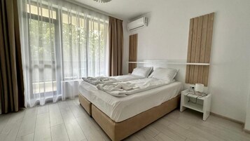 Quarto com cama, mesa de cabeceira, ar condicionado e janela com cortinas.