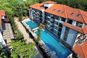 Hotel com vários andares, piscina e área externa com mesas e cadeiras.