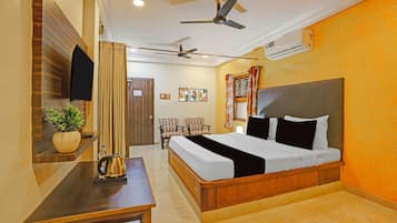 Quarto de hotel com cama, escrivaninha, televisão e ventoinha no teto.