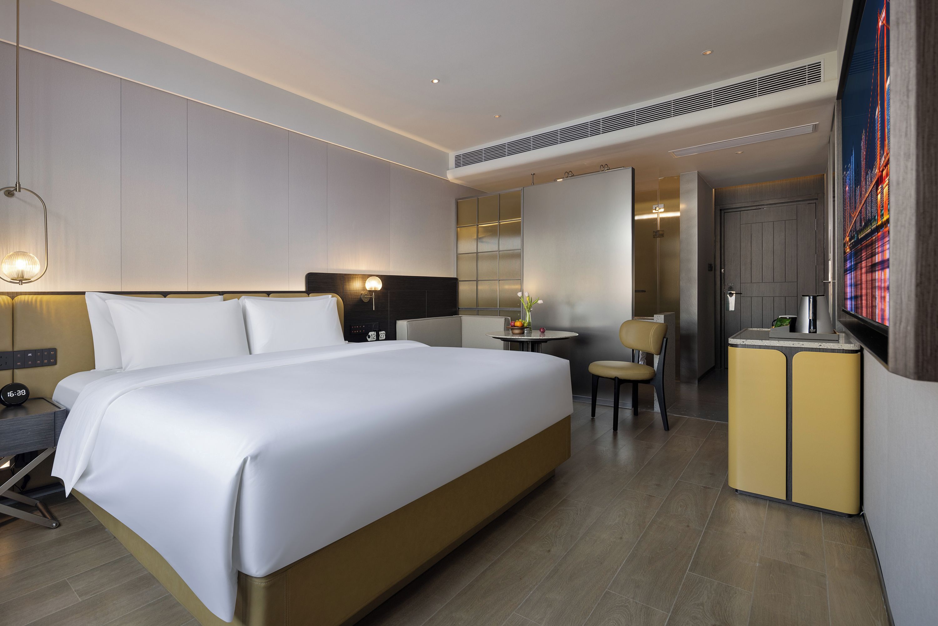 Quarto de hotel moderno com uma cama grande, mesas de cabeceira, escrivaninha, cadeira e espelho.