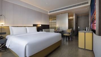 Quarto de hotel moderno com uma cama grande, mesas de cabeceira, escrivaninha, cadeira e espelho.