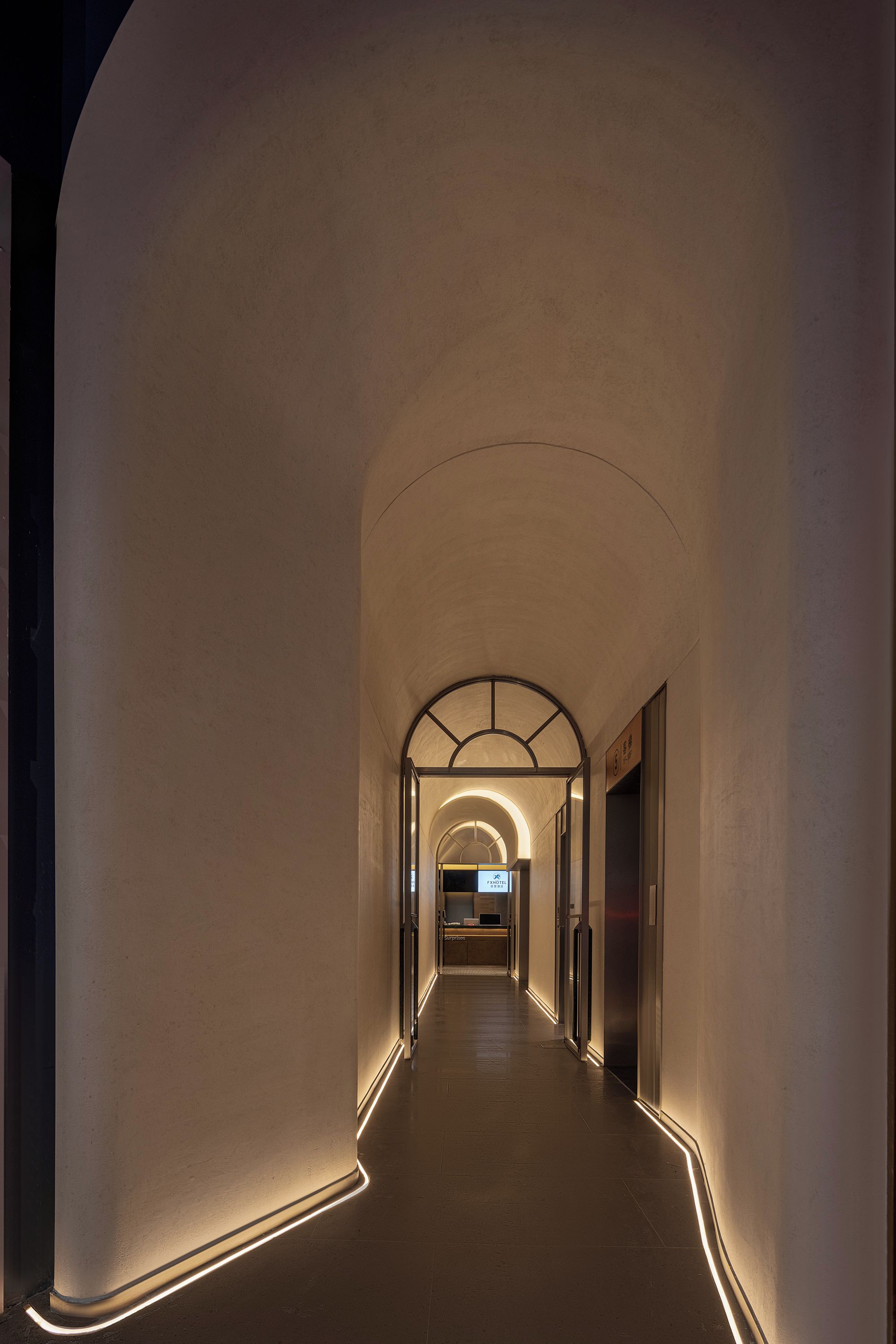 Corredor de hotel com design moderno, apresentando um longo hall com tetos arqueados e um caminho central.
