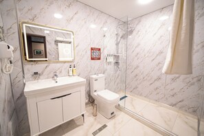 Casa de banho com parede de mármore, lavatório branco, sanita e área de duche.
