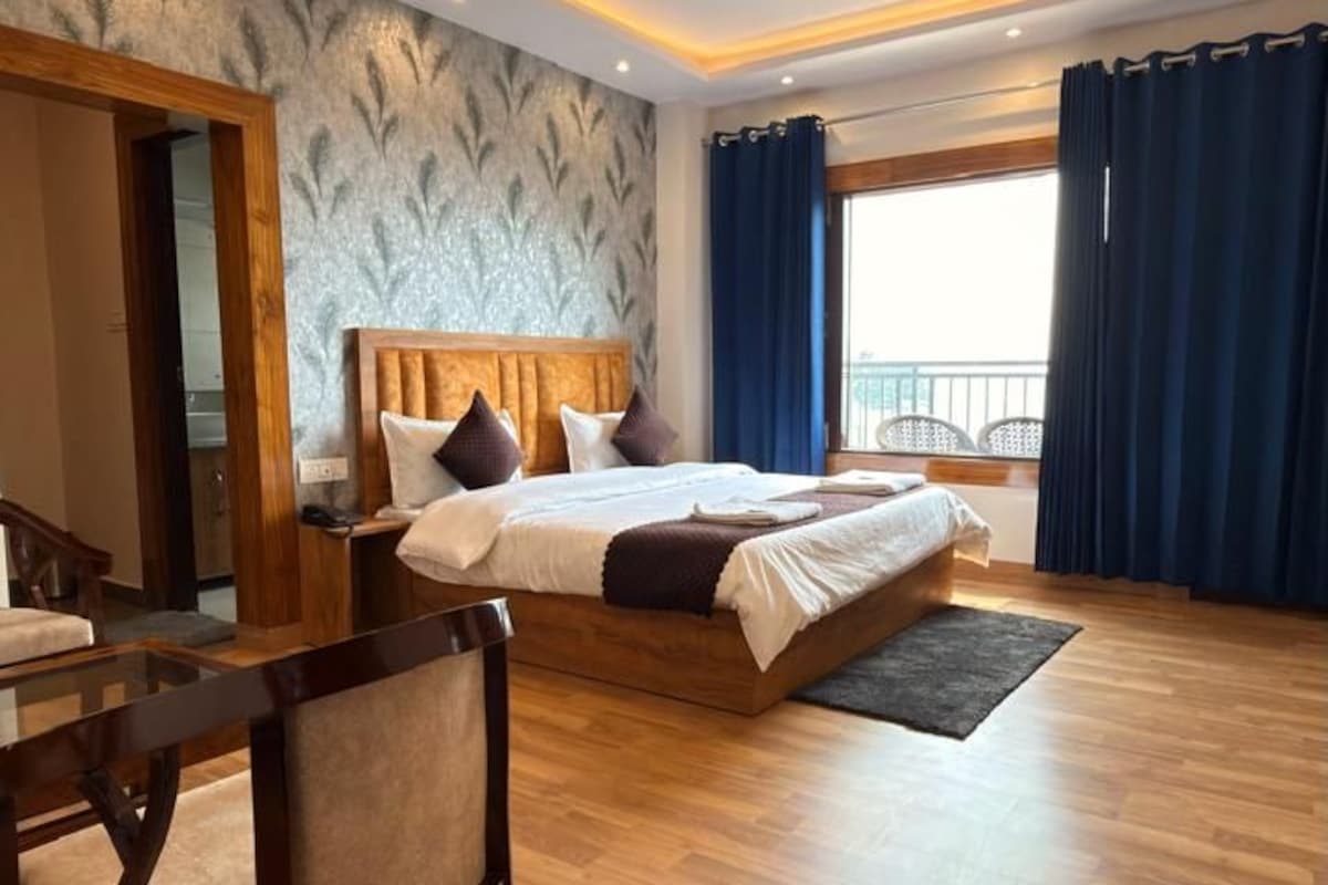 Quarto moderno com cama grande, piso de madeira, luminária circular no teto e vista para o exterior.