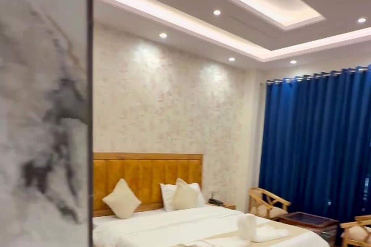 Quarto moderno com cabeceira de madeira, cama grande com roupa de cama branca, tapete preto e cortina azul.