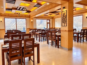 Uma sala de jantar espaçosa com mesas e cadeiras de madeira, amplas janelas com vista para as montanhas e um design de teto acolhedor.
