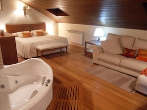 Quarto com uma cama grande, área de estar com sofá, piso de madeira, banheira e radiador.