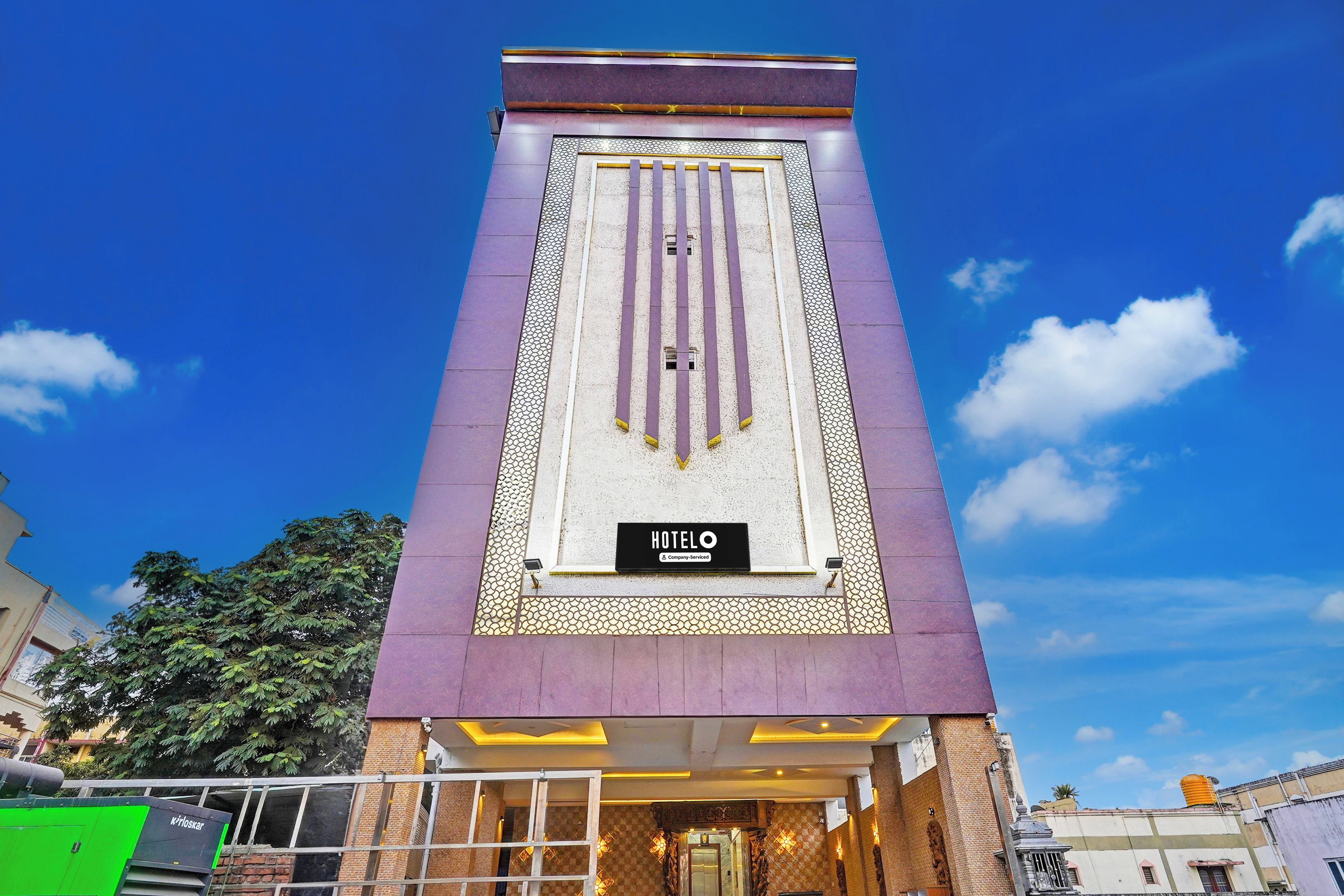 Hotel com uma placa vertical chamativa, fachada estampada e céu azul ao fundo.