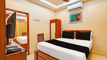 Quarto de hotel com cama, secretária com telefone, televisão, unidade de ar condicionado e um quadro na parede.