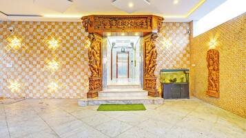 Um saguão de hotel com padrão de piso xadrez, uma escadaria central e um arco de madeira decorativo.