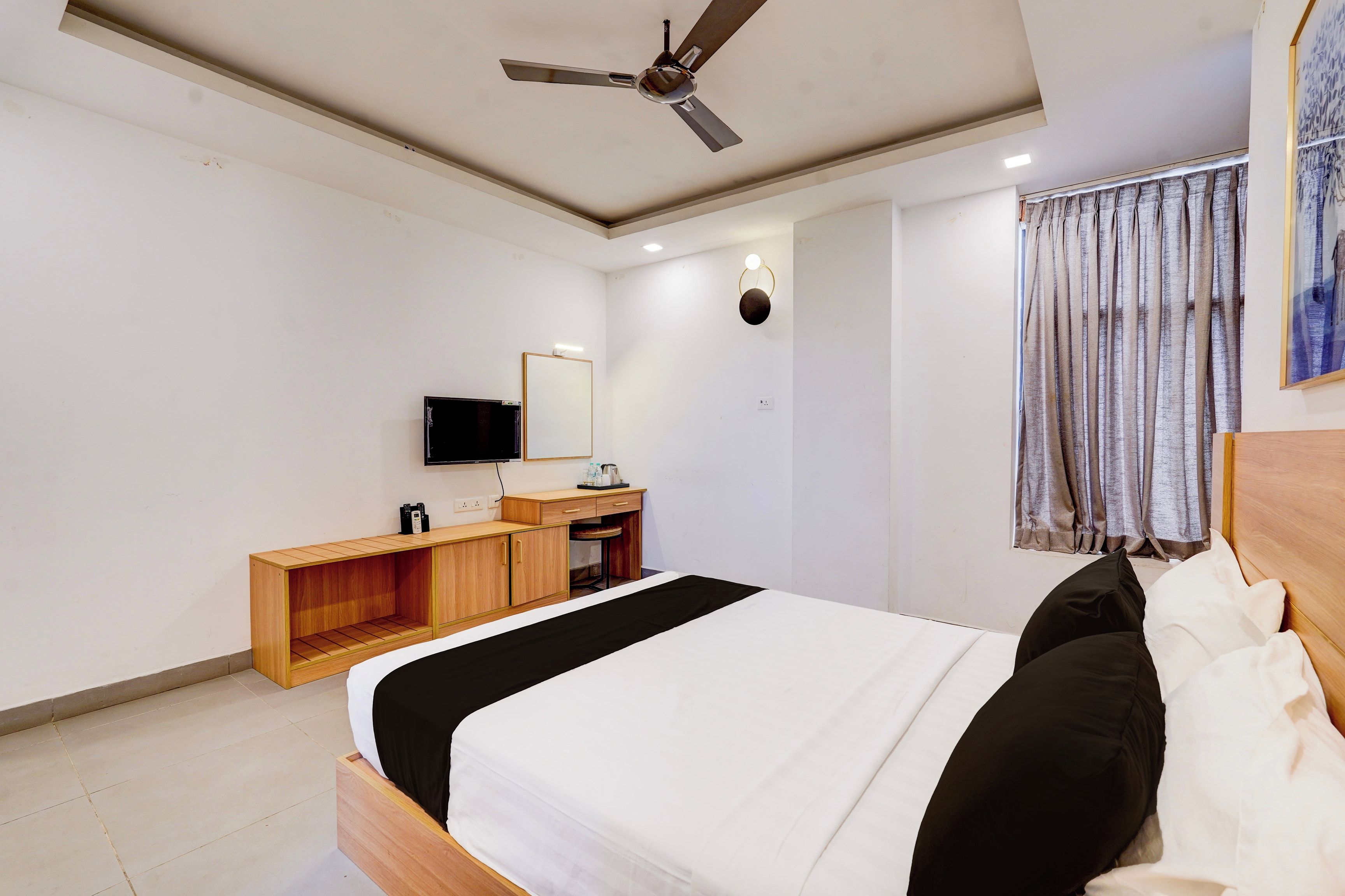 Quarto de hotel com cama, escrivaninha, televisão e ventoinha no teto.