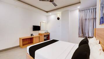 Quarto de hotel com cama, escrivaninha, televisão e ventoinha no teto.