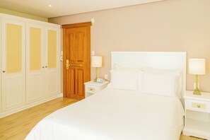 Quarto de hotel com uma cama grande, duas mesas de cabeceira com luminárias, um guarda-roupa de madeira e uma porta.