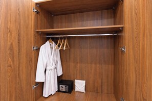 Um closet espaçoso com paredes de madeira, um roupão pendurado em um cabide, um cofre e uma toalha dobrada no chão.