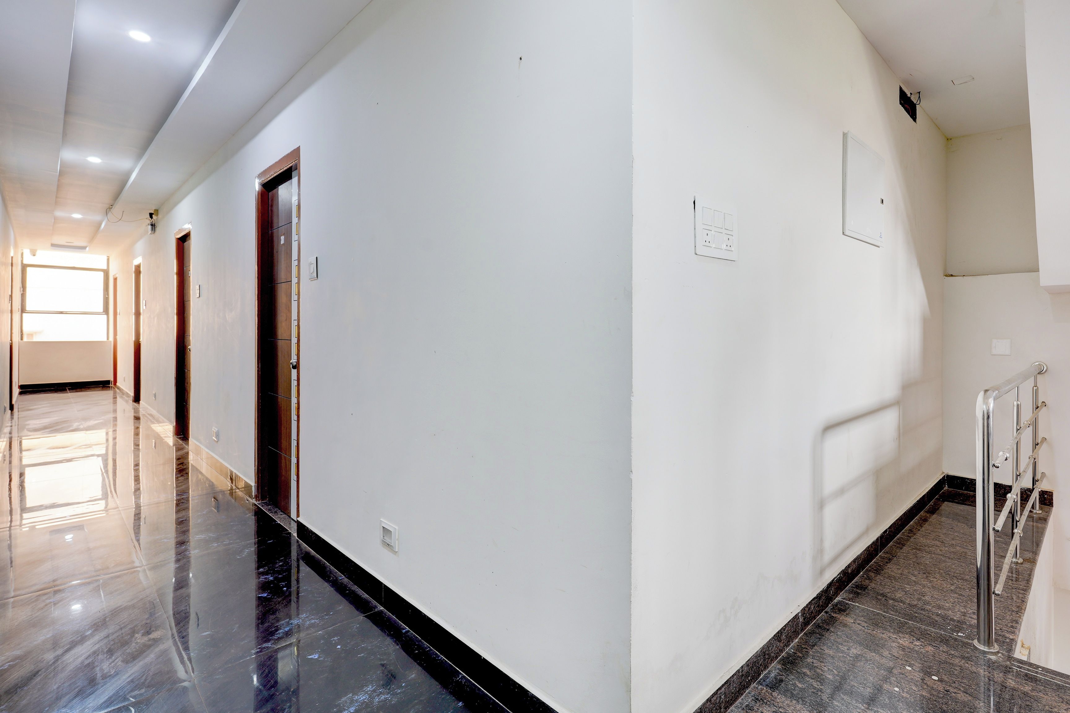 Corredor com paredes brancas, piso de mármore e corrimão de metal.