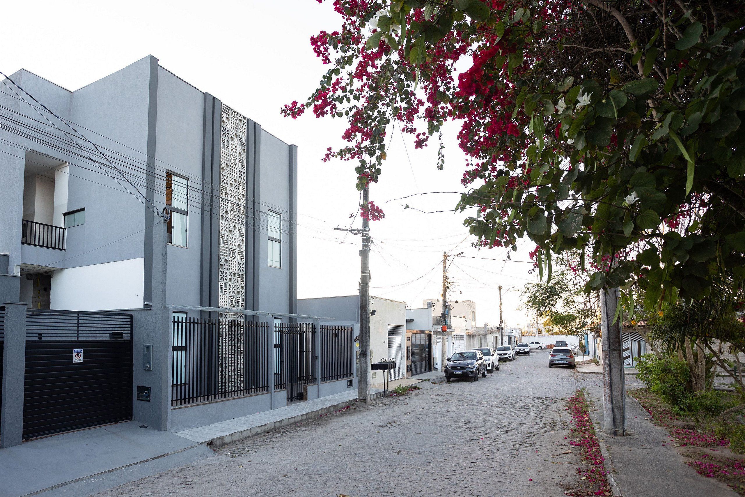 Uma rua estreita em área urbana, com edifícios modernos, portão e carros estacionados.