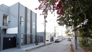 Uma rua estreita em área urbana, com edifícios modernos, portão e carros estacionados.