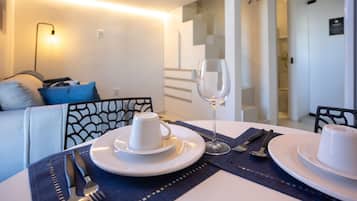 Uma área de refeições com uma mesa posta para dois, incluindo pratos, uma xícara, uma taça de vinho e talheres.