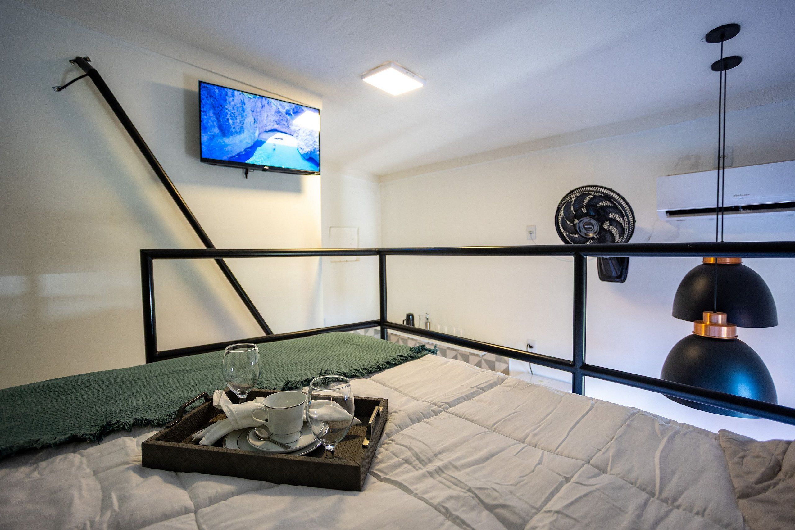 Quarto de hotel moderno com cama, TV de tela plana na parede, ventilador de teto e janela com vista.
