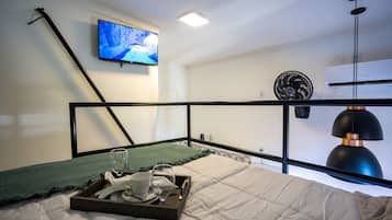 Quarto de hotel moderno com cama, TV de tela plana na parede, ventilador de teto e janela com vista.