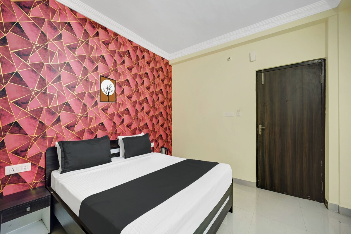 Quarto de hotel com cama, mesa de cabeceira, relógio na parede e porta.