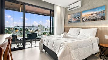 Quarto de hotel moderno com varanda ampla, cama com roupa de cama branca e duas pinturas da paisagem urbana na parede.