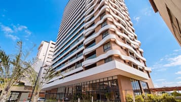 Um edifício moderno de grande altura com fachada ondulada única, amplas janelas e área de entrada ajardinada.