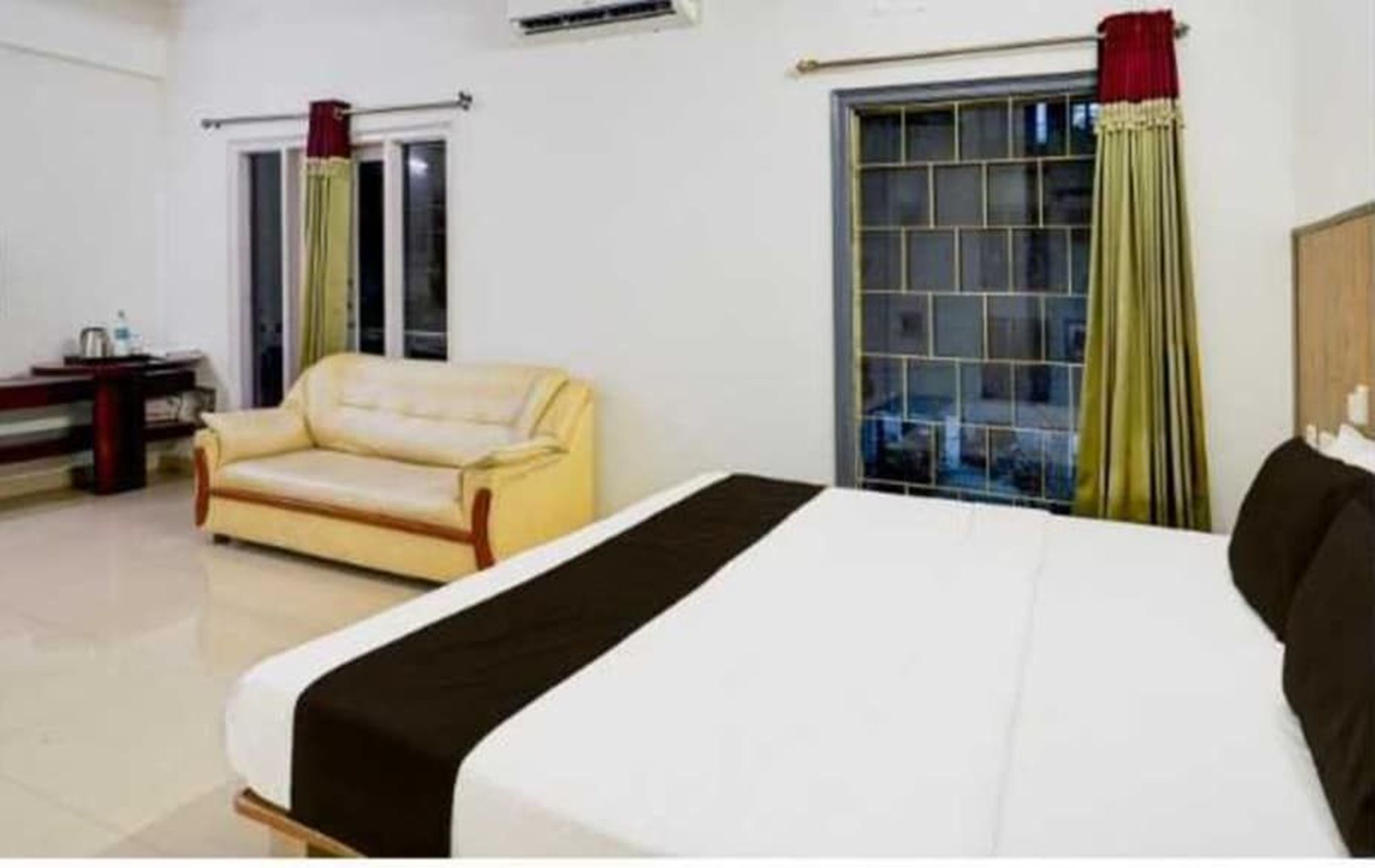 Quarto de hotel com cama, sofá, escrivaninha e janela com cortinas.