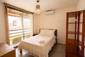 Quarto de hotel com cama, mesa de cabeceira, luminária, guarda-roupa e janela com persianas.