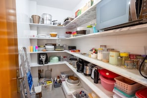 Cozinha com armários brancos, diversos eletrodomésticos e recipientes de armazenamento.