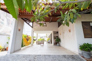 Espaço coberto ao ar livre com terraço, assentos e plantas em vasos.