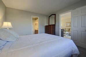 Quarto com cama, penteadeira, espelho e porta que dá para outro cômodo.