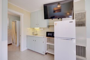 Cozinha compacta com armários brancos, micro-ondas, geladeira e televisão fixada na parede.
