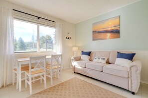 Quarto com sofá, mesa de jantar com cadeiras, luminária e pintura de pôr do sol.