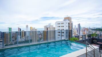 Piscina no terraço com vista para a cidade, cercada por edifícios.