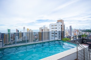 Piscina no terraço com vista para a cidade, cercada por edifícios.