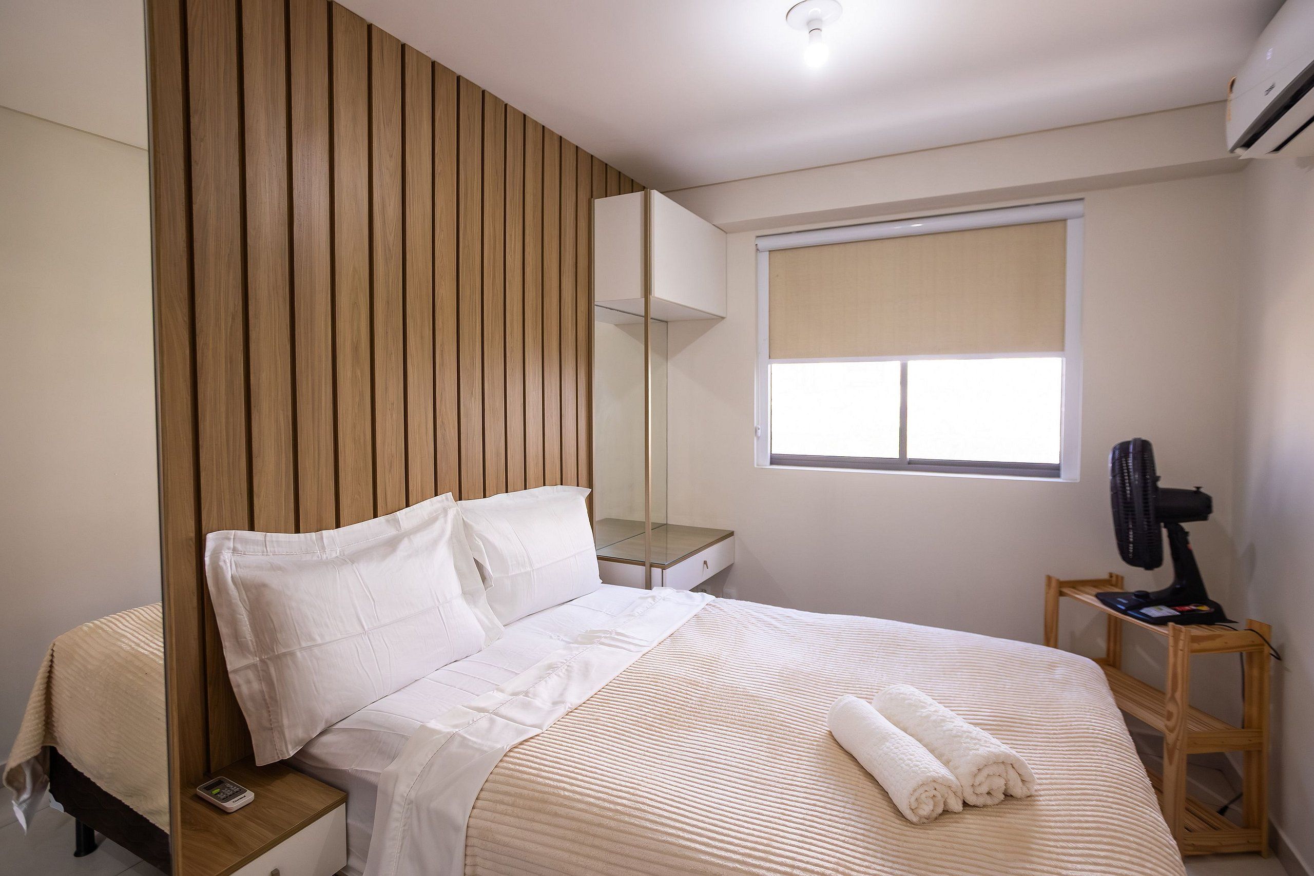 Quarto de hotel com cama, mesa de cabeceira, escrivaninha, cadeira, janela com vista e ar condicionado.