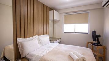 Quarto de hotel com cama, mesa de cabeceira, escrivaninha, cadeira, janela com vista e ar condicionado.